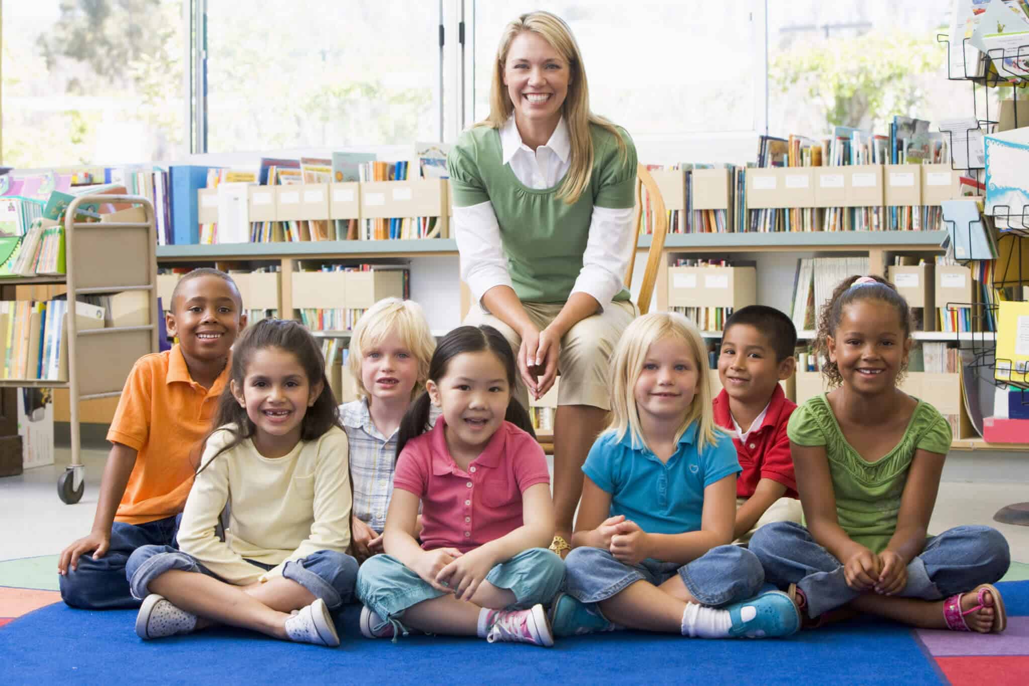 Kindergarten teacher sitting with children in library - iCare Childcare ...